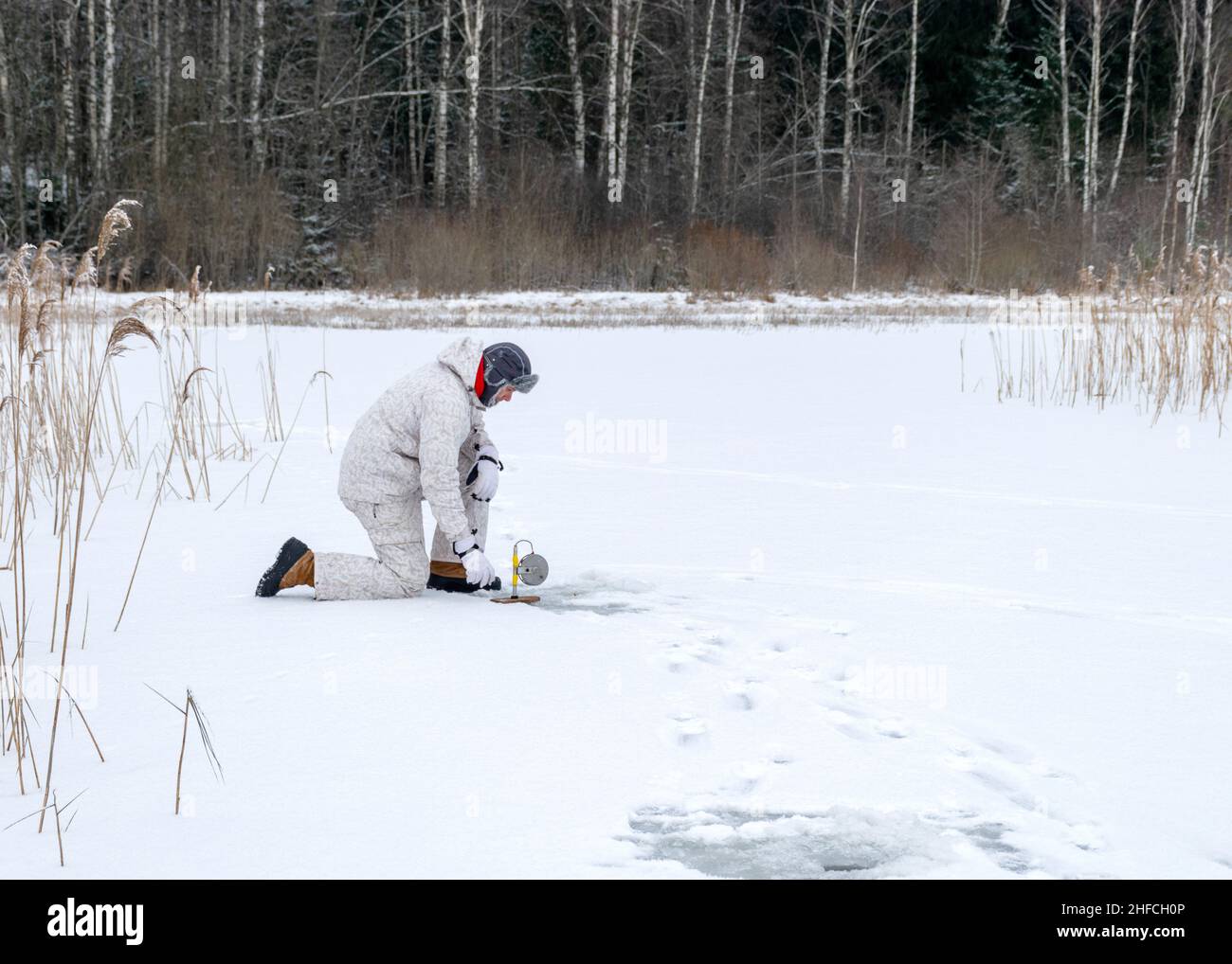 A lone ice fishing man sits on a snowy lake and catches fish. Winter ...