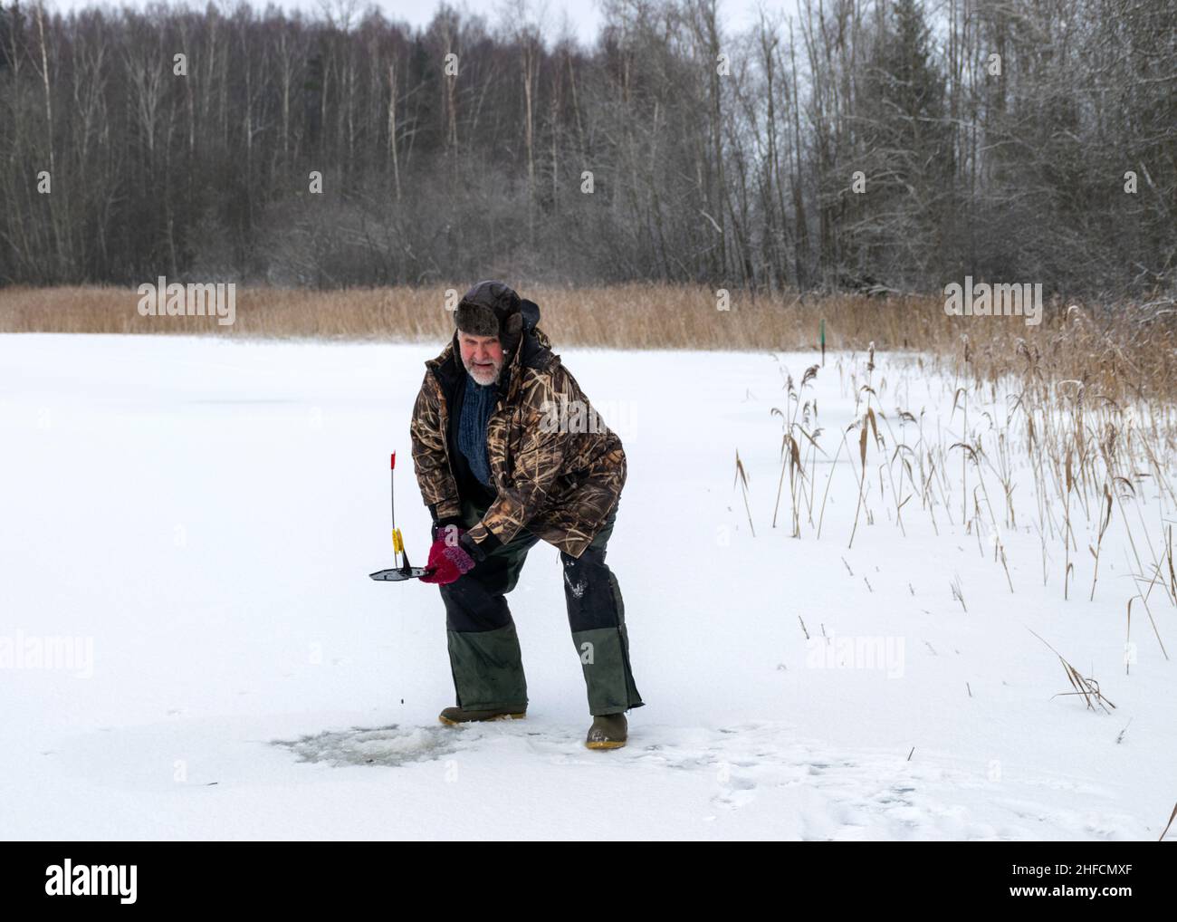 A lone ice fishing man sits on a snowy lake and catches fish. Winter ...