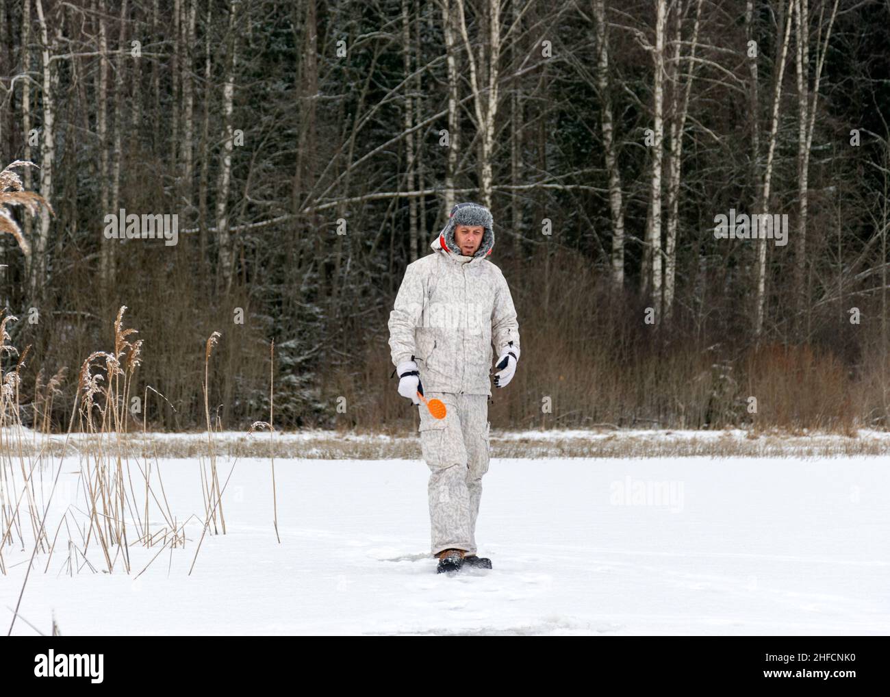 A lone ice fishing man sits on a snowy lake and catches fish. Winter ...