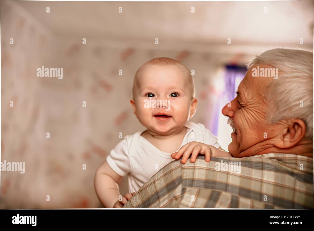 A smiling old man holds a child in his arms. Elderly man keeps a ...