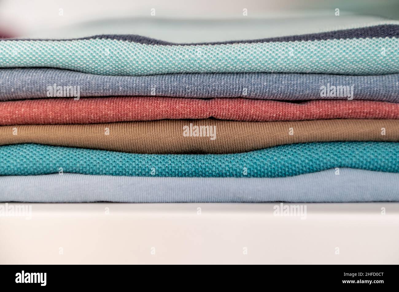 Closeup photo of neatly folded colorful clothes on shelf in wardrobe ...