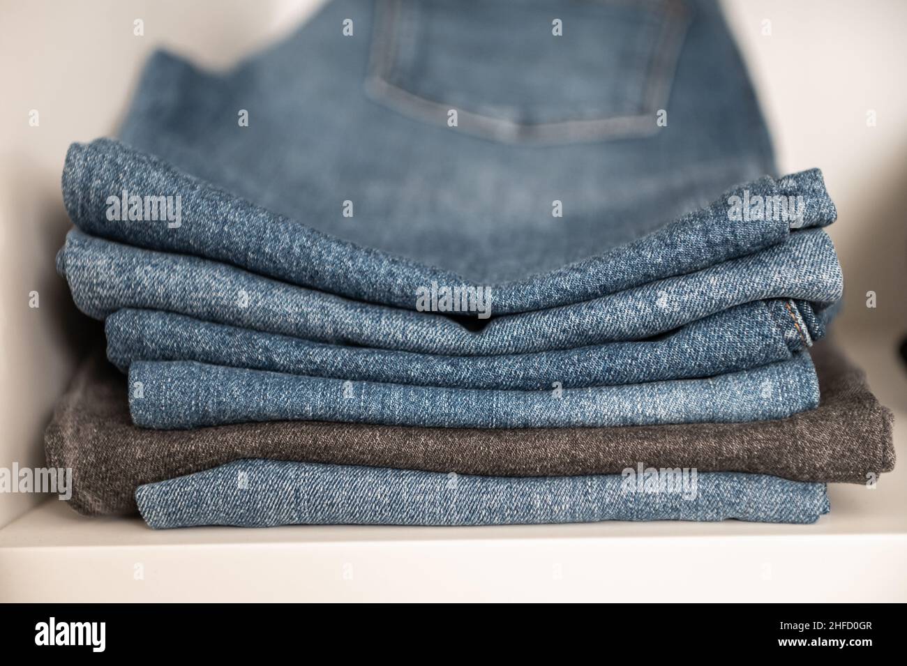 Closeup photo of pile of neatly folded blue jeans on shelf in wardrobe ...