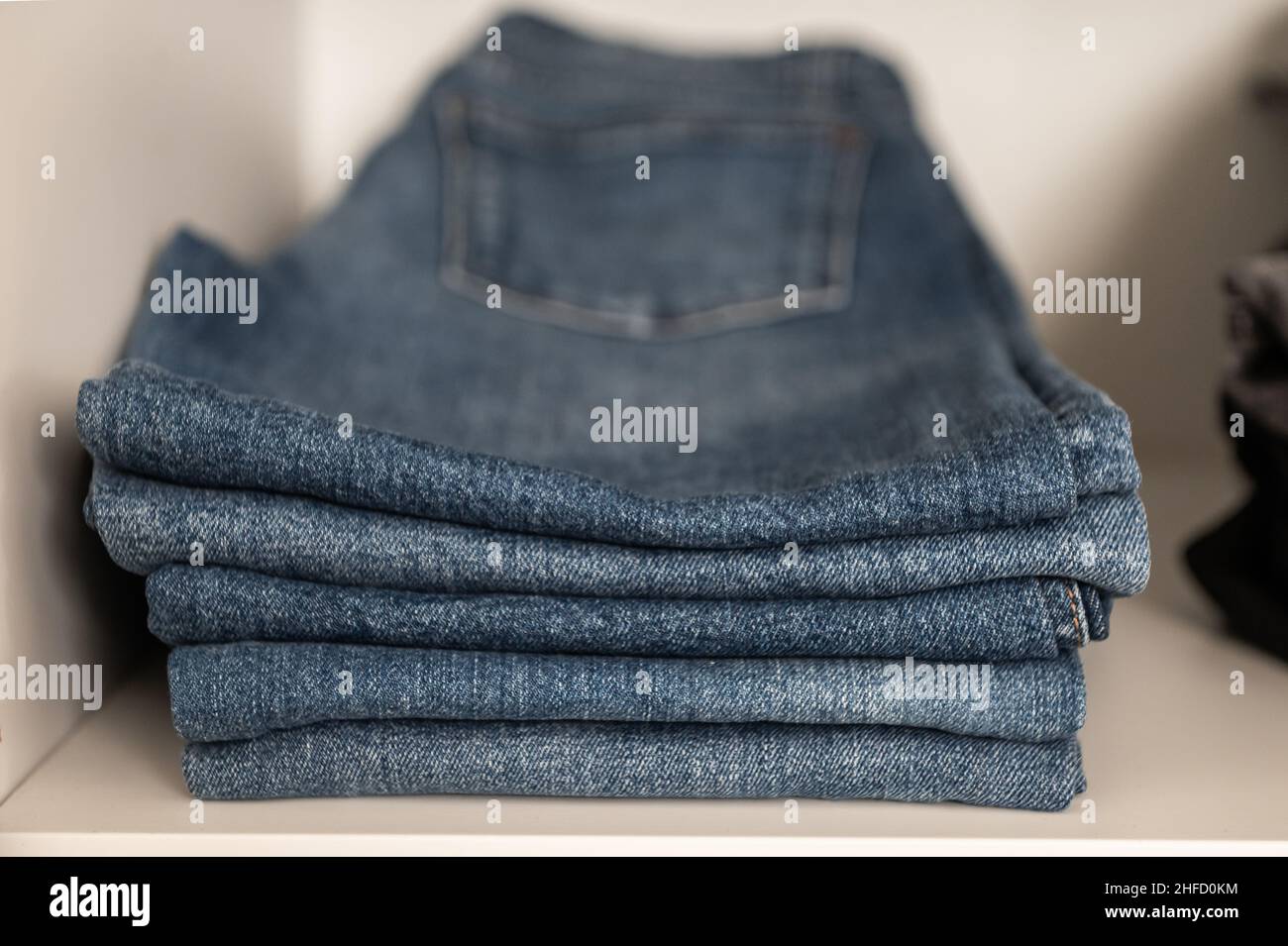 Closeup photo of pile of neatly folded blue jeans on shelf in wardrobe ...