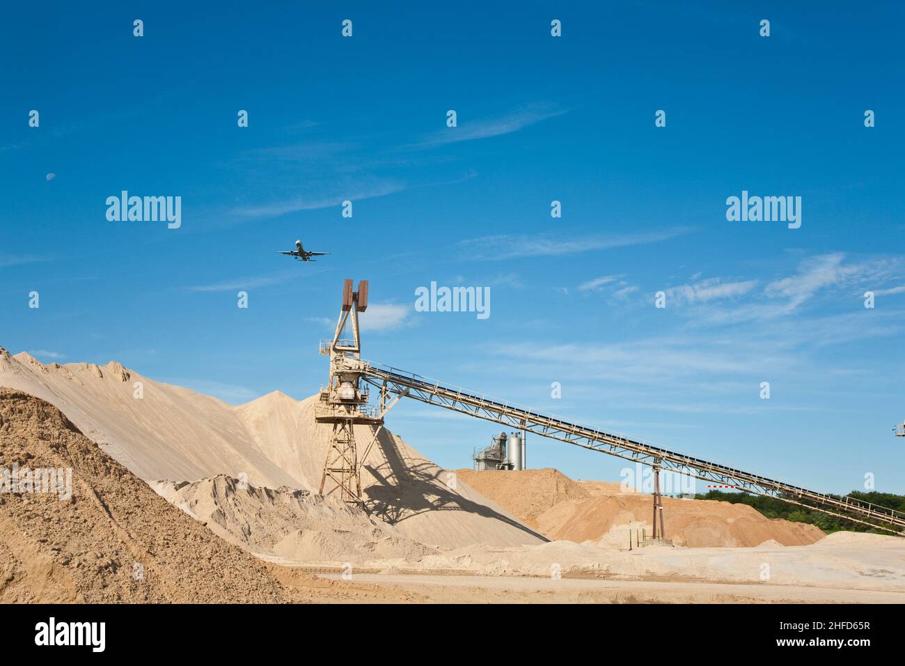 Conveyor on site at gravel pit hill with overflying aircraft in ...