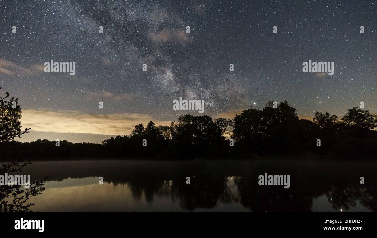 Milky Way at night over a small lake with silhouette of trees on the ...