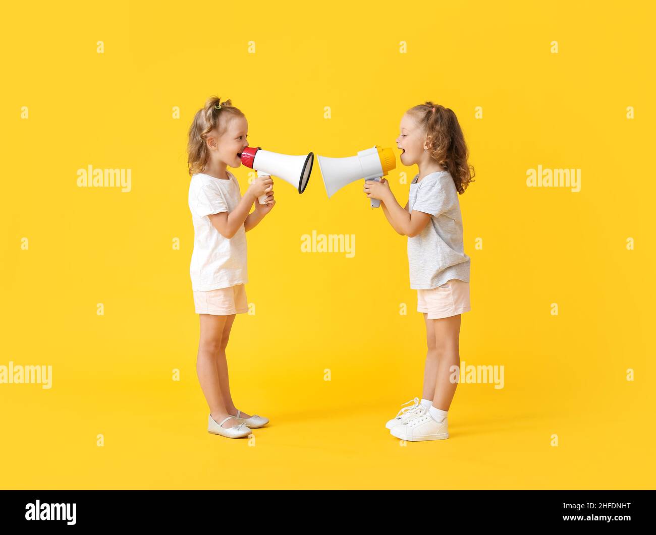 Cute little girls shouting into megaphones on yellow background Stock ...