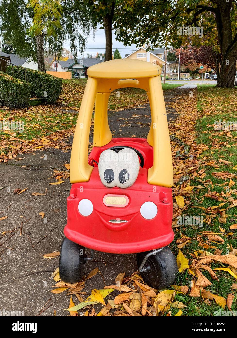 A Brightly Colored Childs Car on a leaf lined autumn sidewalk Stock ...