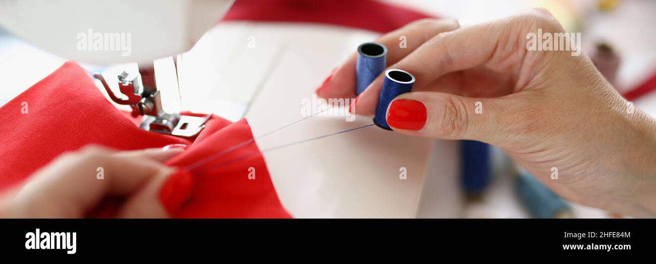 Seamstress hands hold blue thread and red cloth Stock Photo - Alamy