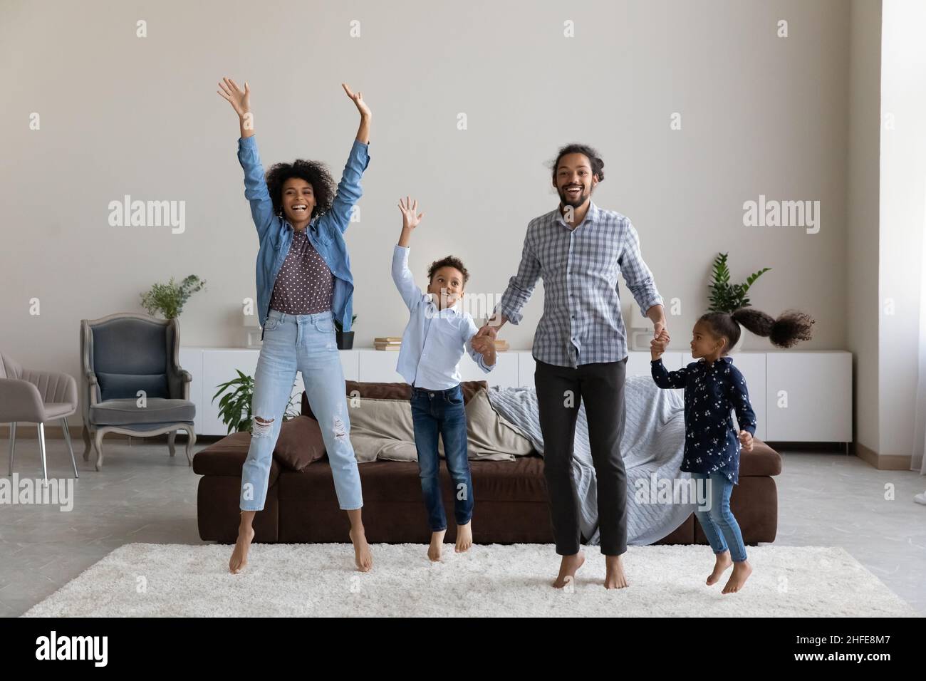 Excited cheerful African parents and little kids jumping on carpet ...