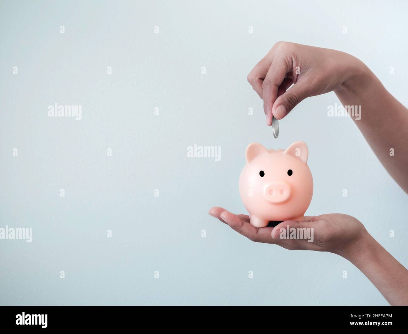 Money box on hand. Hand puts coin into the pink piggy bank on hand ...