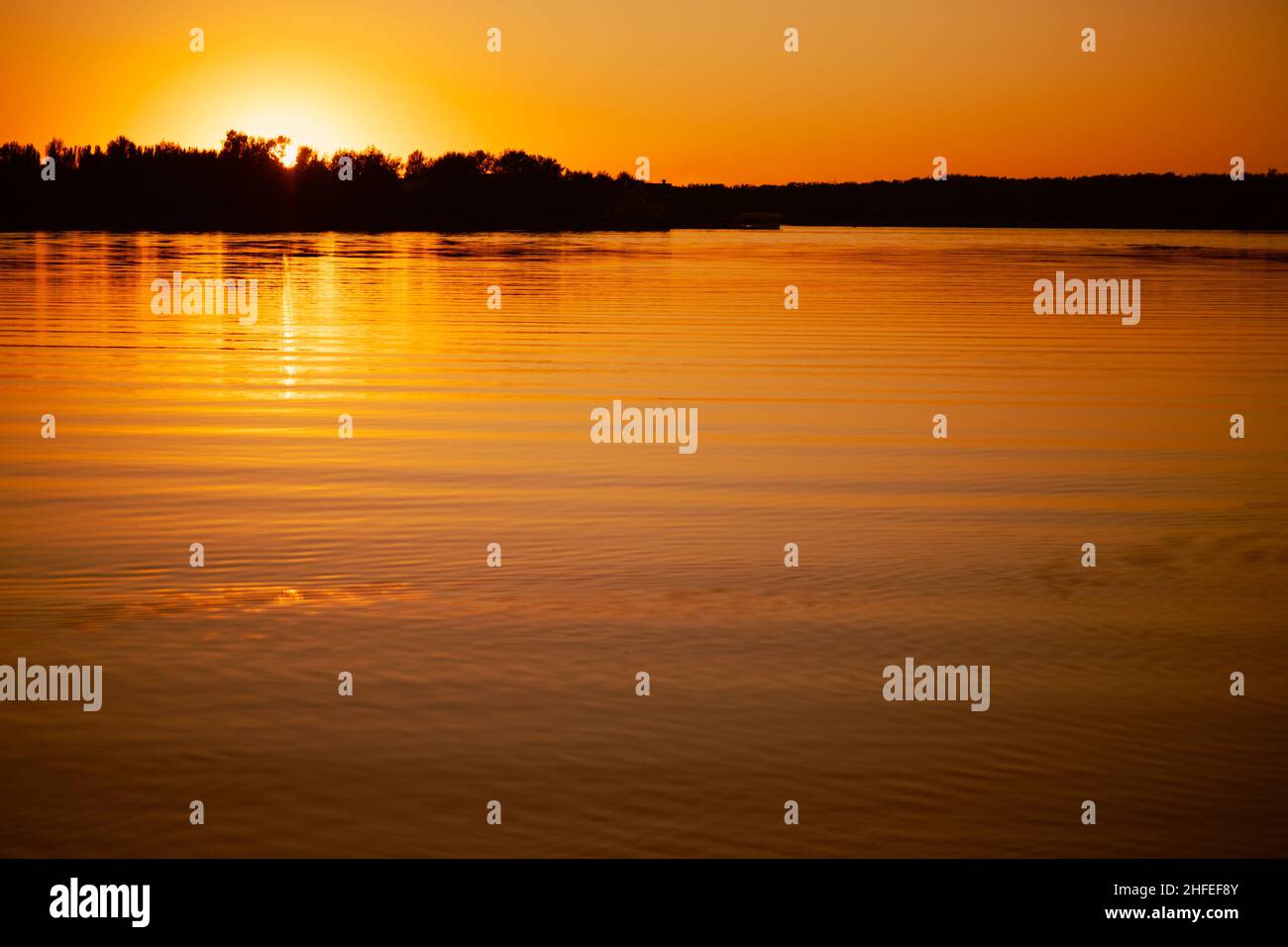 Shining lake with sun setting below horizon and covering with rays ...