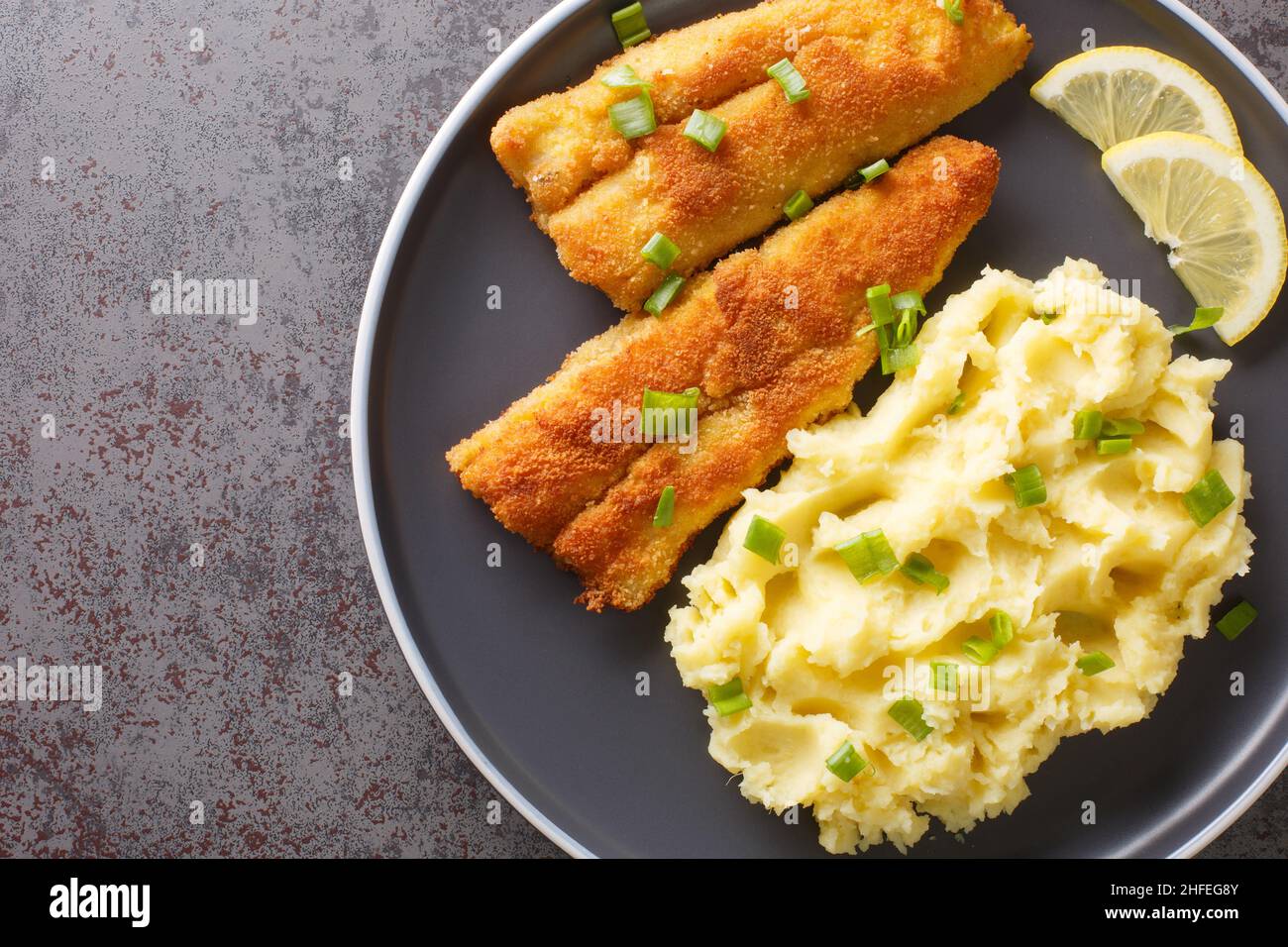 Fried fish fillet and mashed potatoes, lemon close-up in a plate on the ...