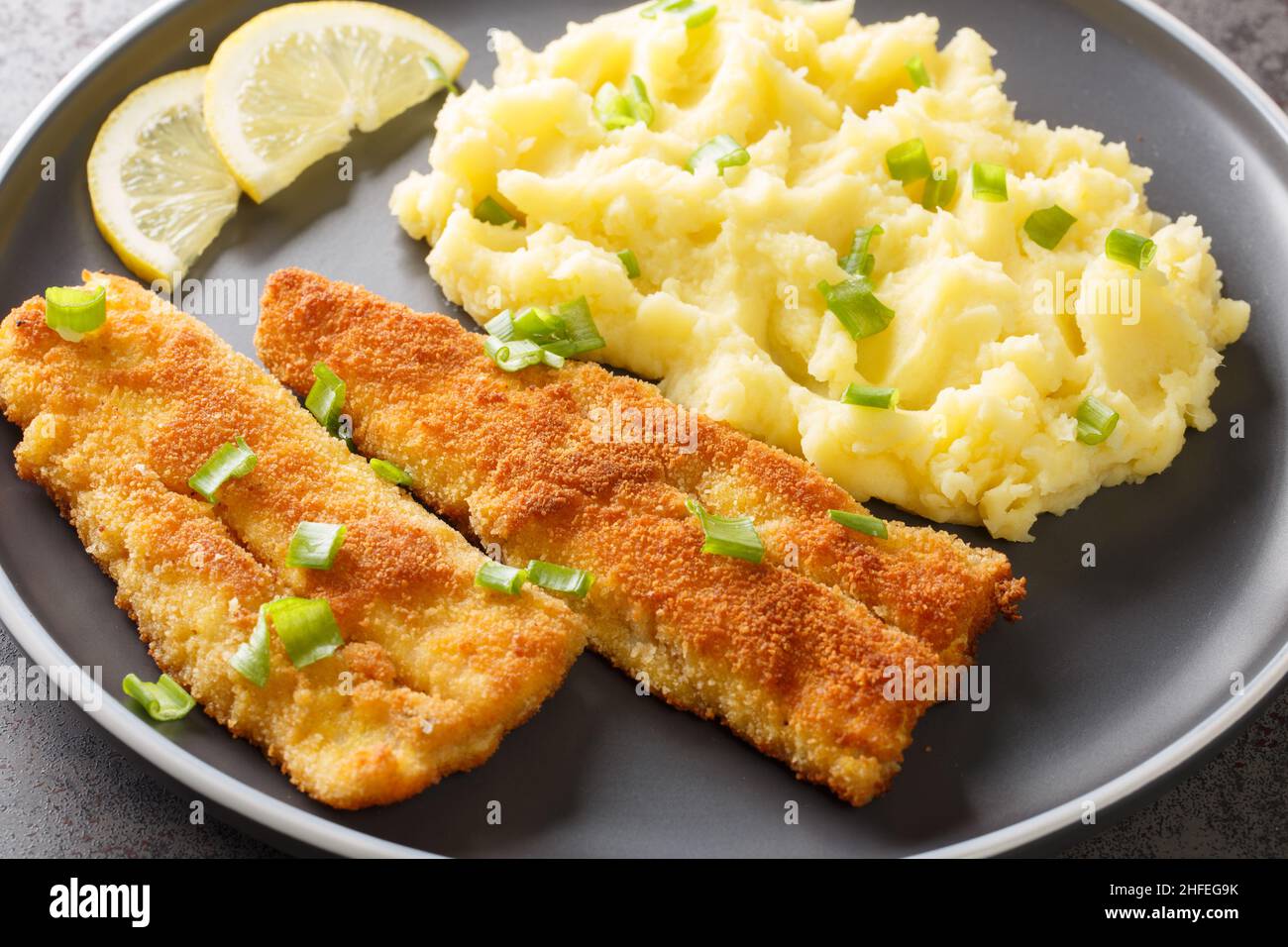 Fried fish fillet and mashed potatoes, lemon close-up in a plate on the ...