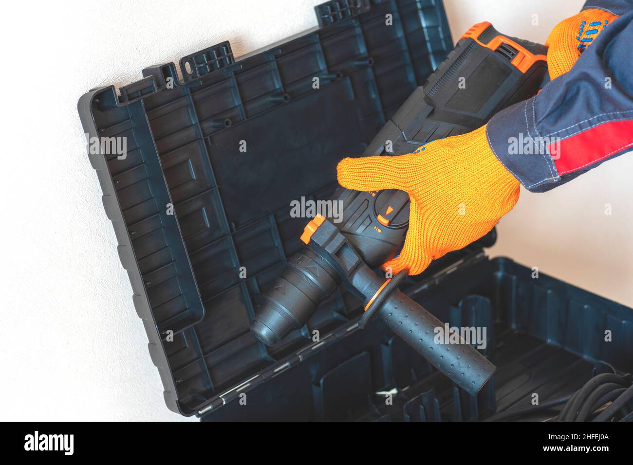 Hands in protective gloves hold a rotary hammer. worker, professional ...