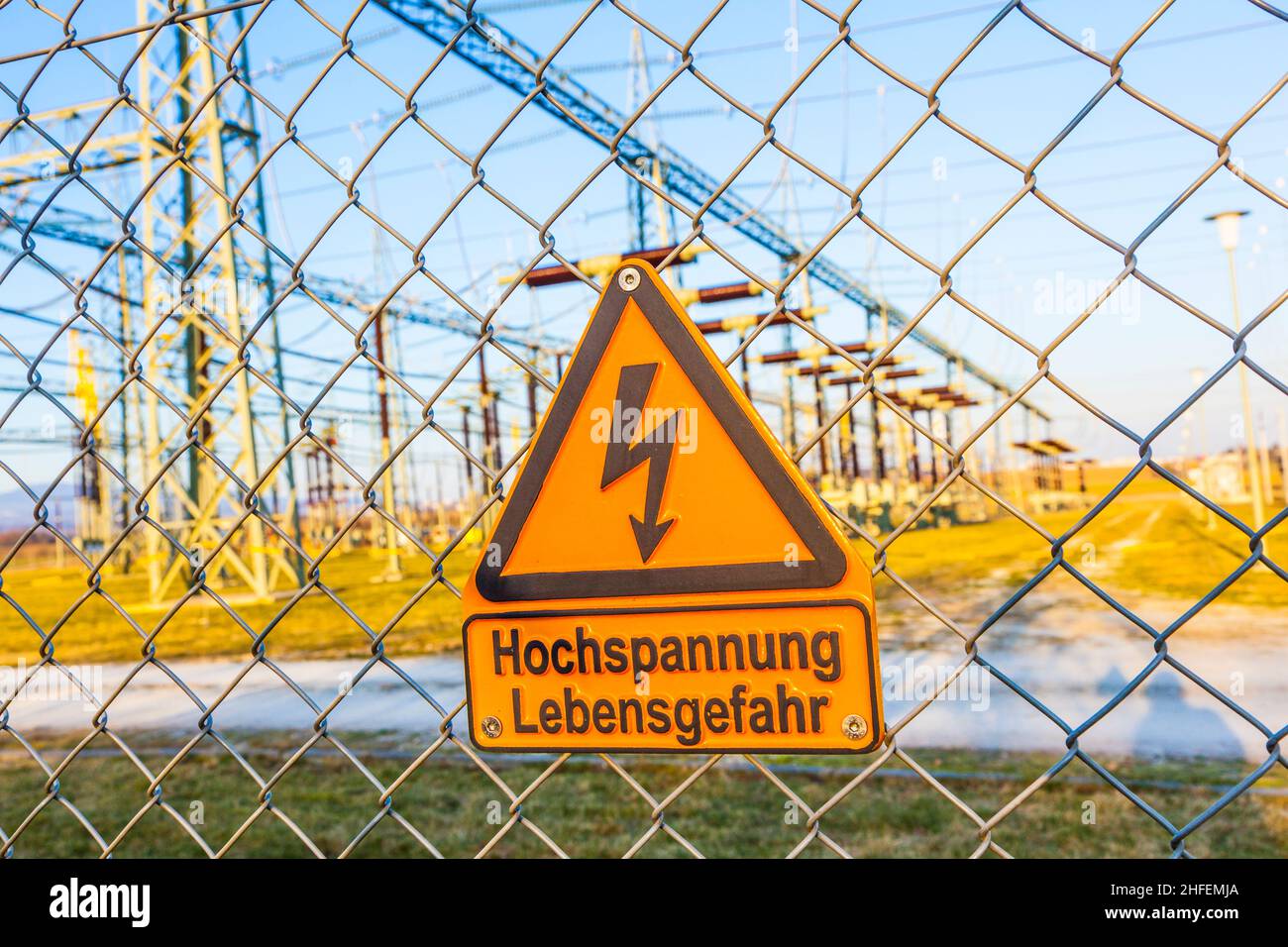 warning sign at hight voltage tower in rural landscape with blue sky ...