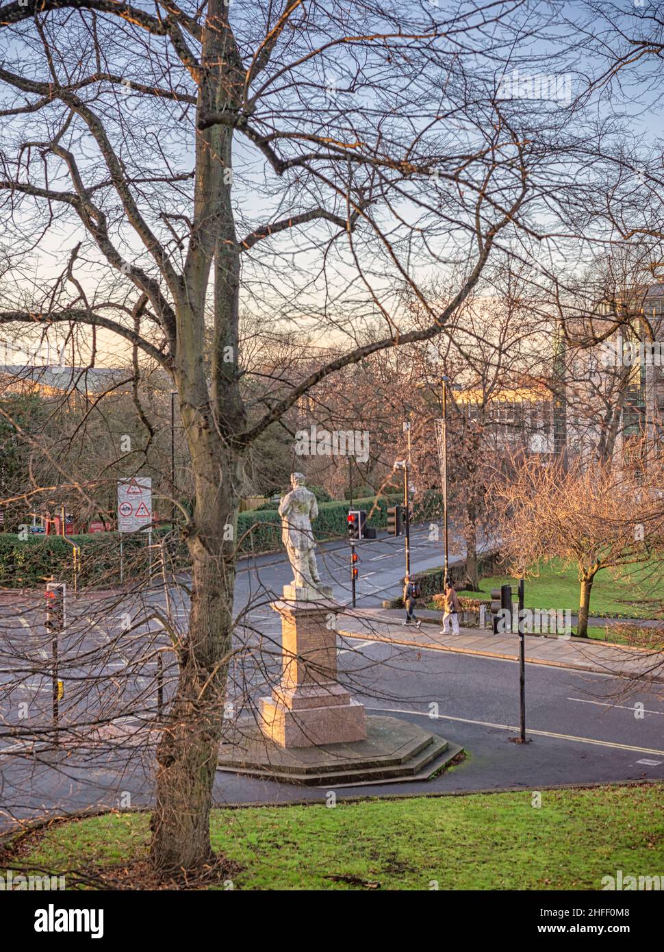 A statue stands at a road junction with a large tree in the foreground ...