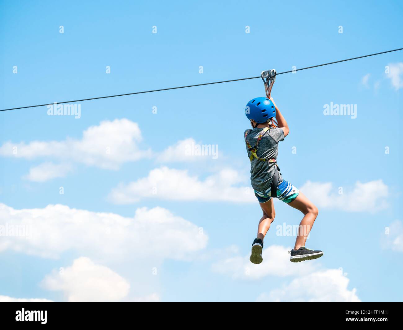 Back view with a teen young adult riding a zip line against blue sky in ...