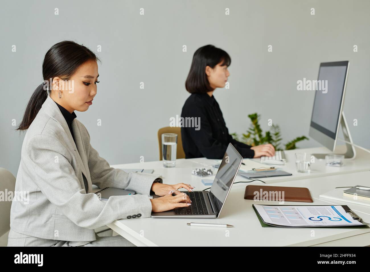 Minimal side view portrait of two young Asian women using computers in ...