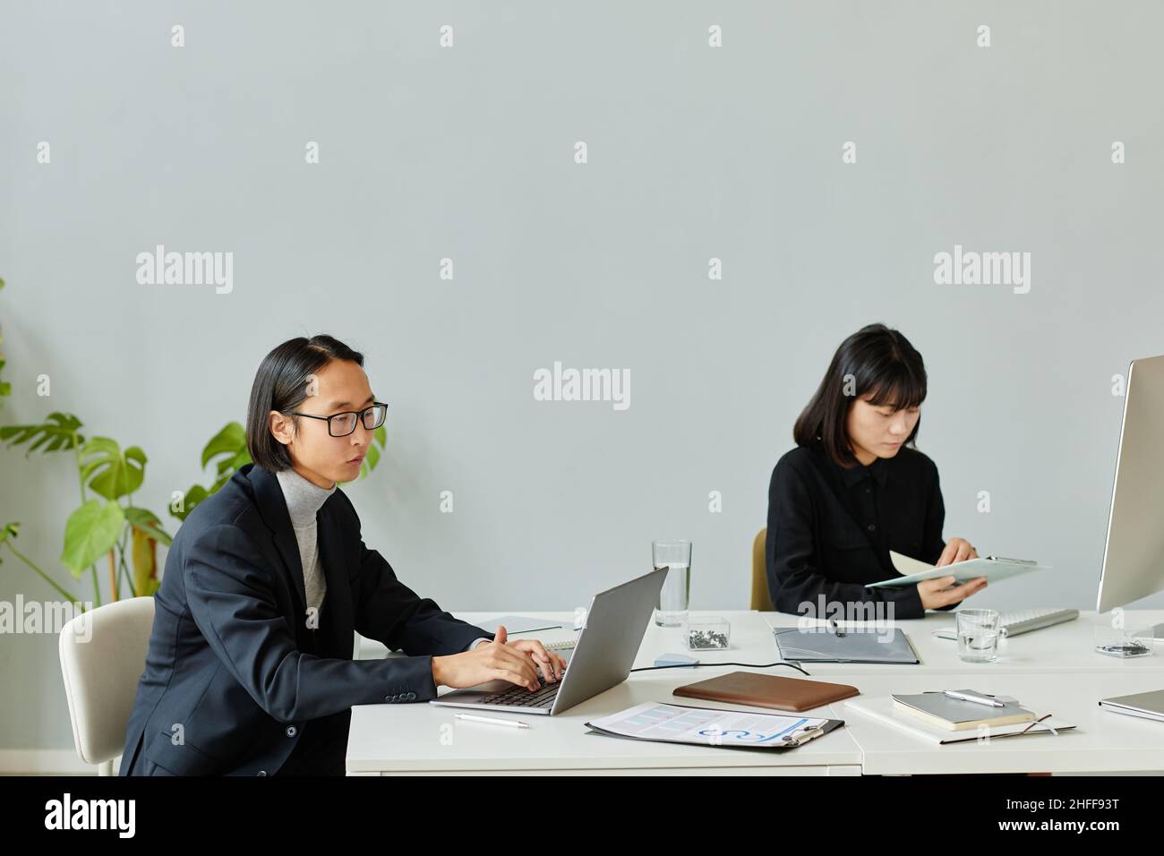 Minimal portrait of two young Asian business people using computers in ...