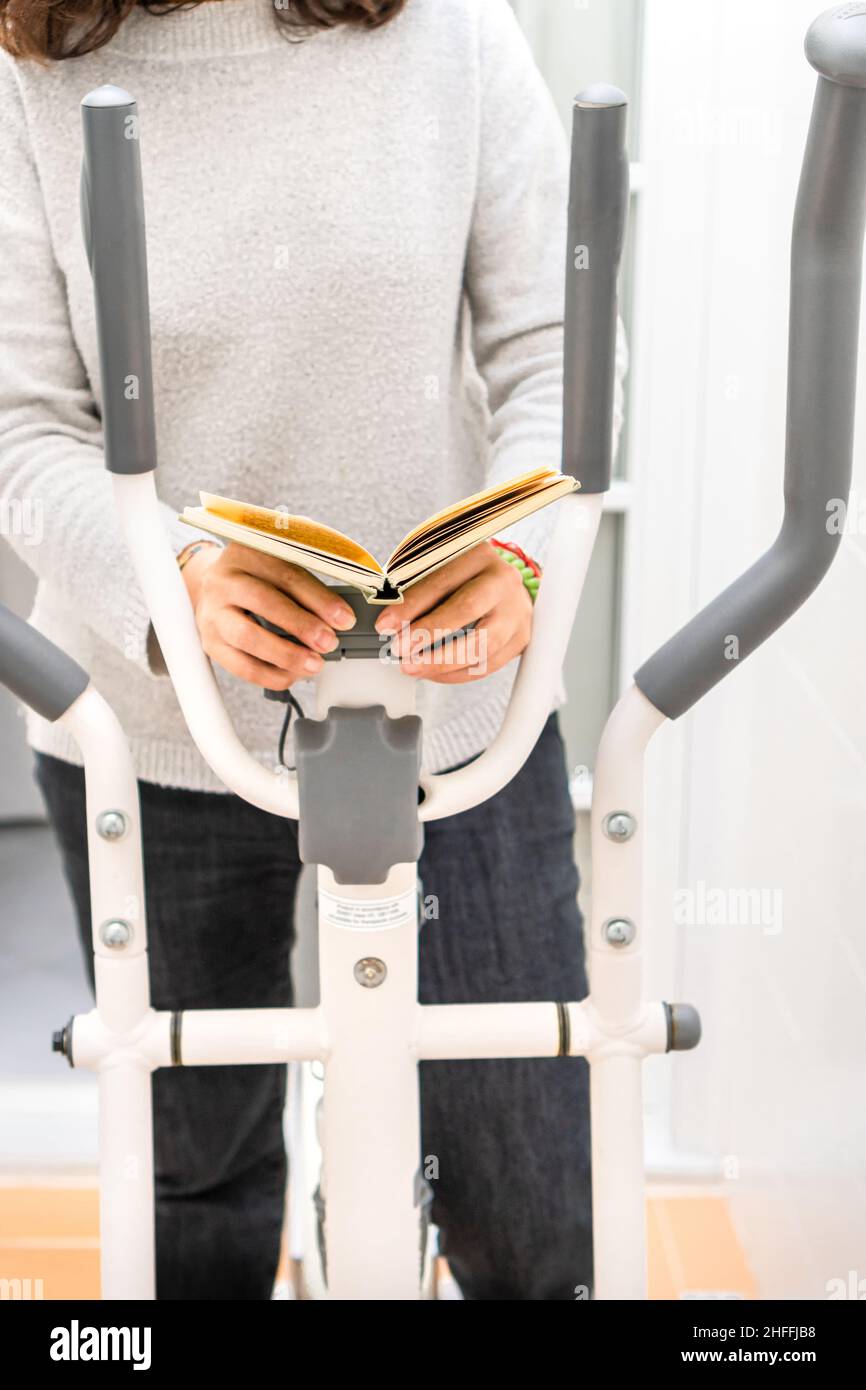 Unrecognized woman exercising on an elliptical bike while reading a ...