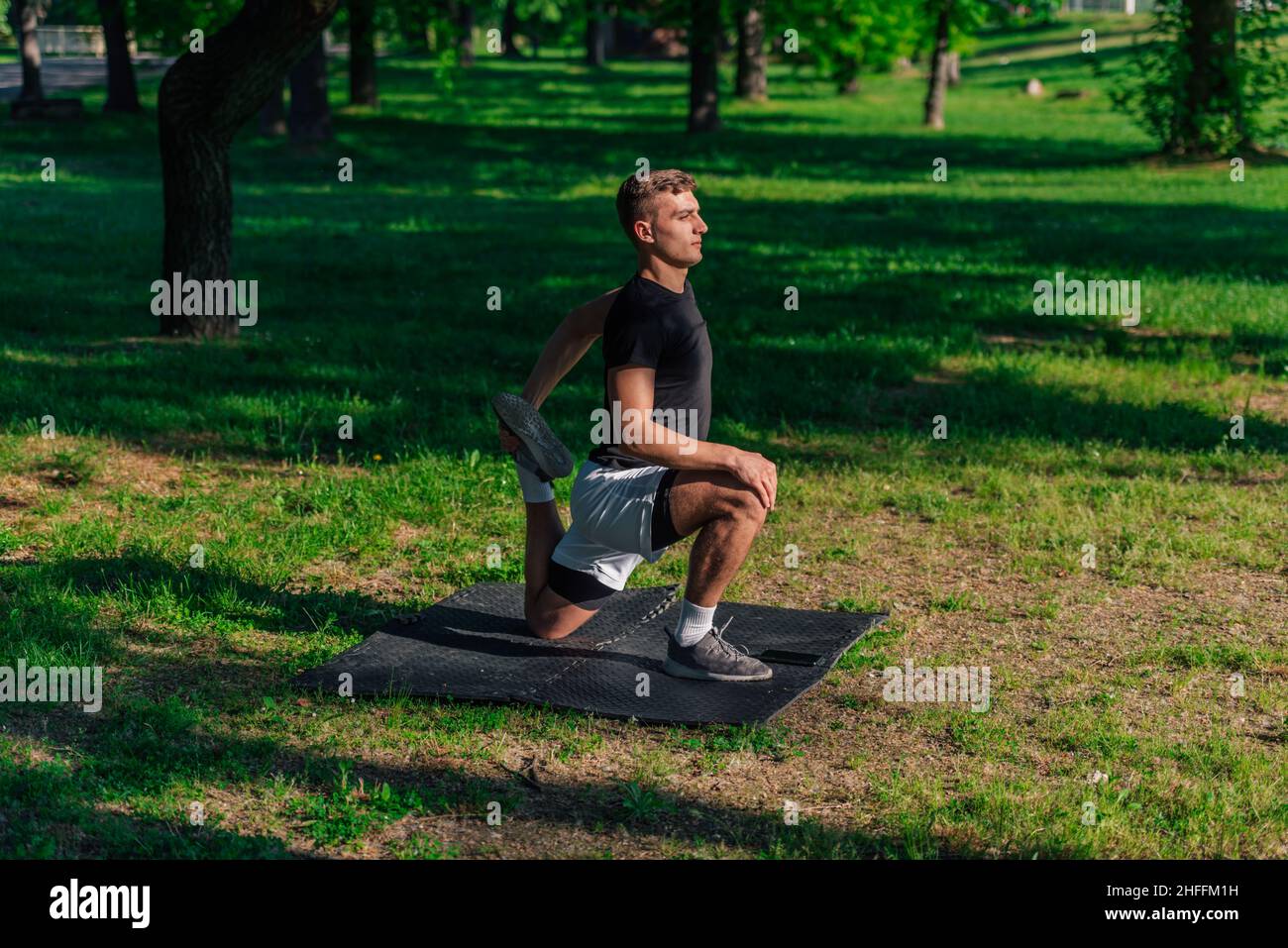 Sporty young man stretching legs and doing forward lunge while having ...