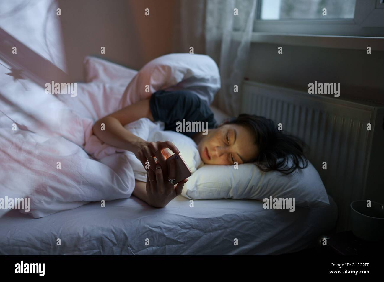 Young depressed woman in bed staring at smartphone screen, feeling ...