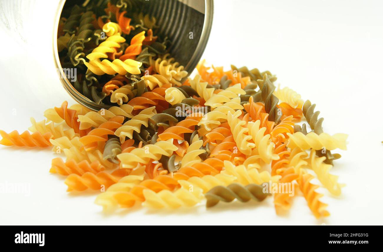 Tin with colorful pasta spirals on dry leaves on white background Stock ...