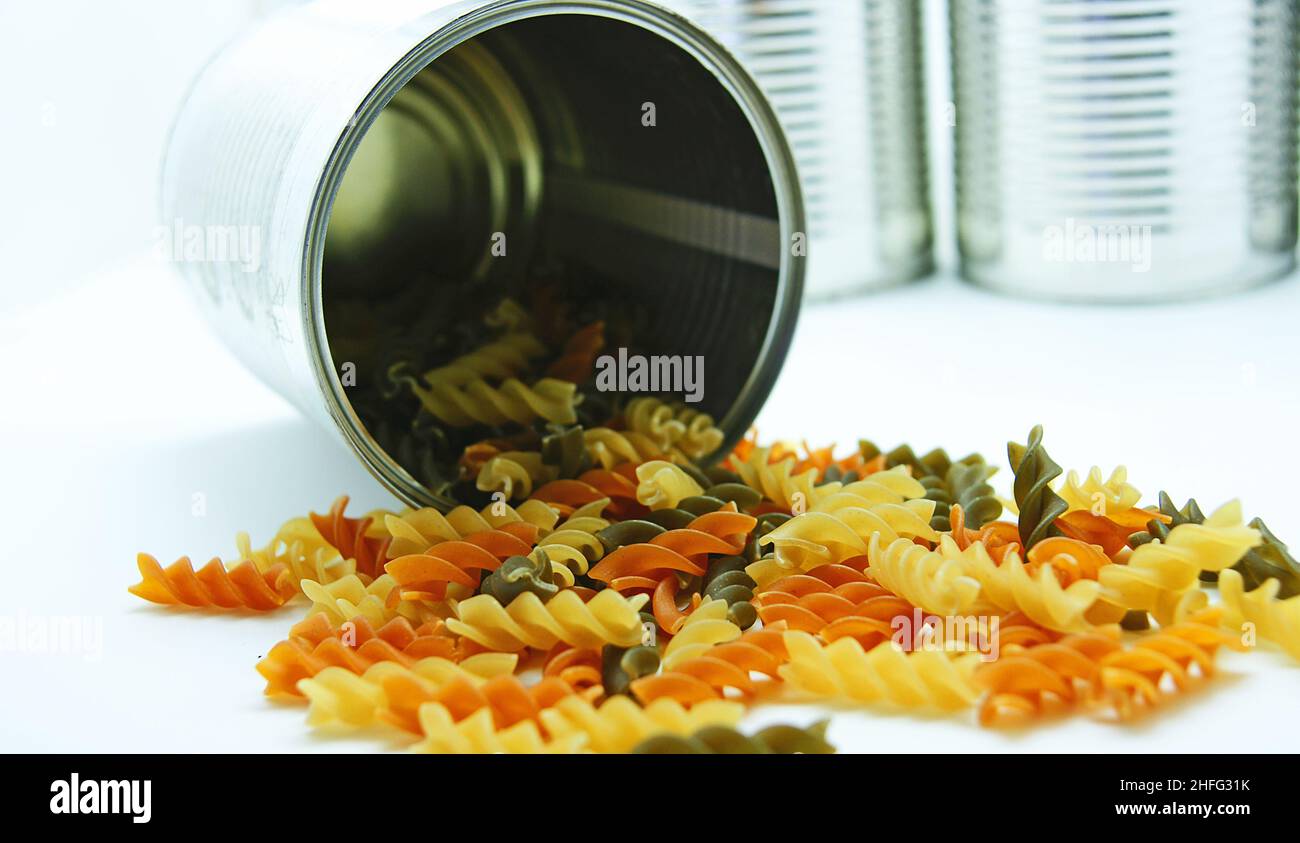 Tin with colorful pasta spirals on dry leaves on white background Stock ...