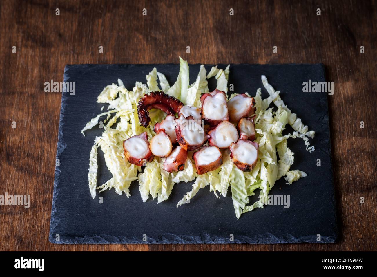 Dried octopus leg on a bed of cabbage on a stone plate with a wooden ...