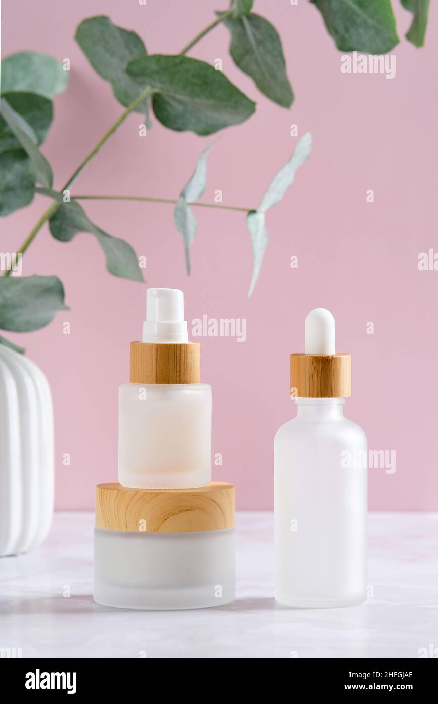 Elegant cosmetics containers and eucalyptus in vase on pink background ...