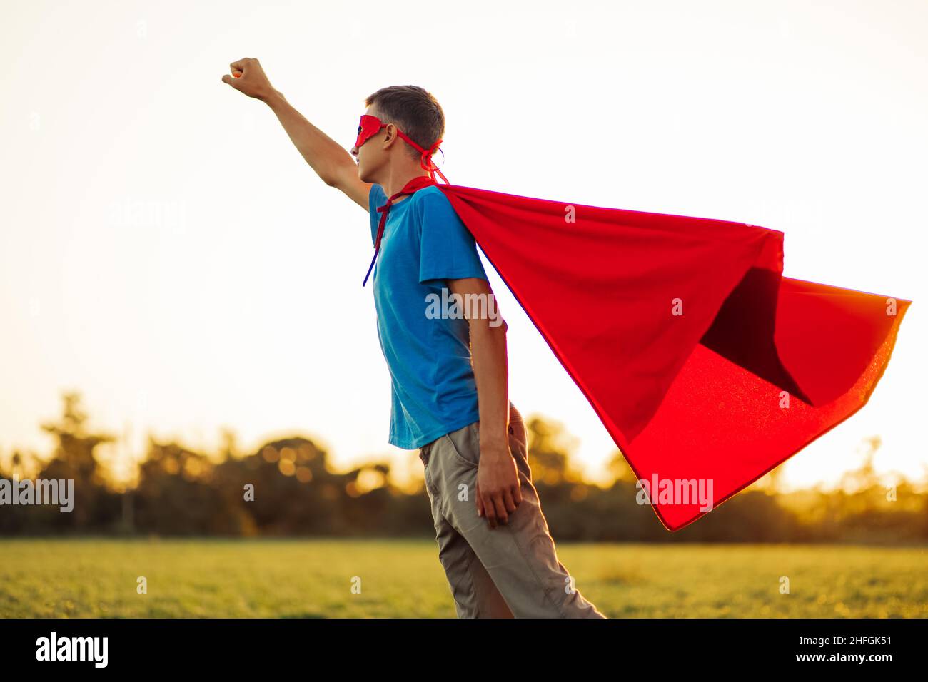 Joyful courageous man in a superhero costume poses on the field against ...