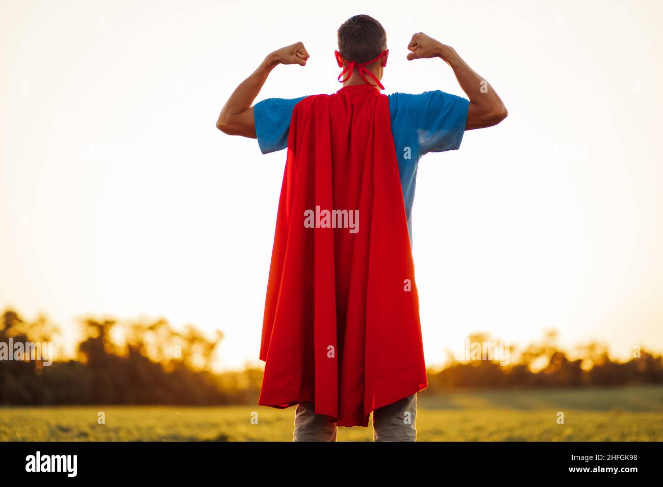 Back view. Successful hero wearing superhero cape, raising arms ...