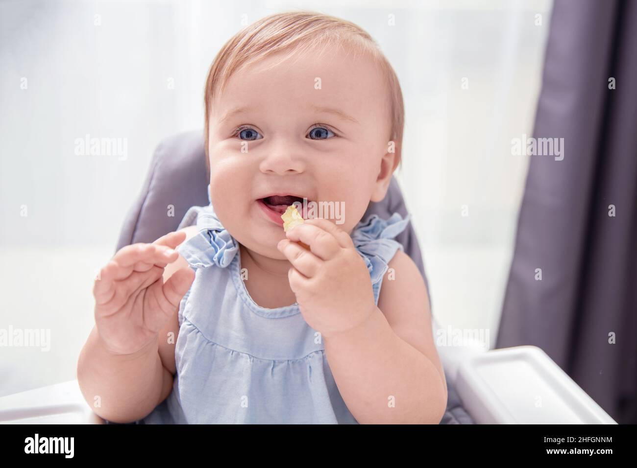 Infant baby girl in blue dress eats crisp and smiles Stock Photo - Alamy