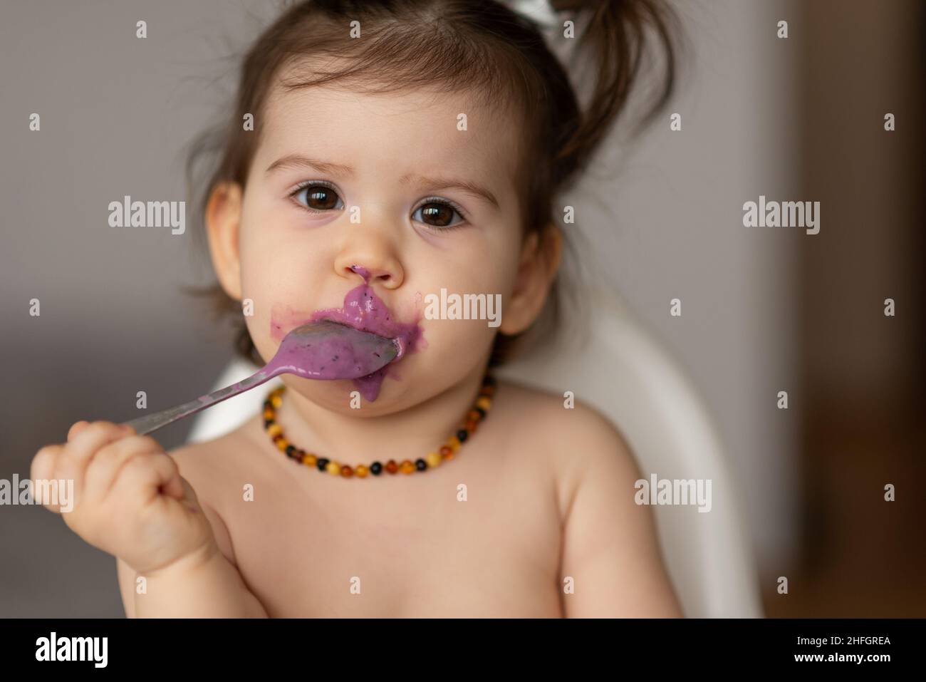 Cute little baby girl eating purple blueberry yogurt with spoon Stock ...