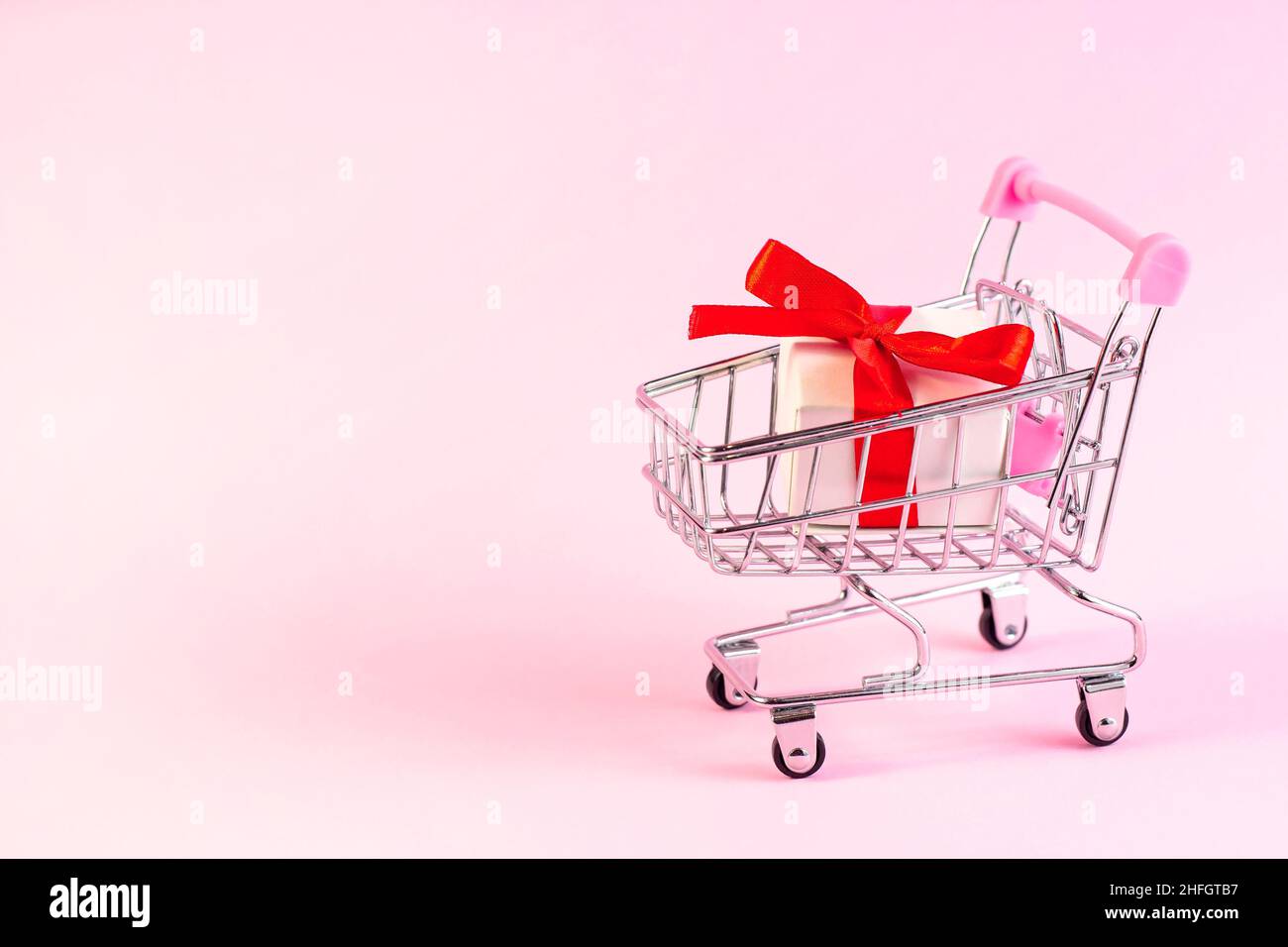 Bright pink shopping trolley push cart with white gift box on light ...