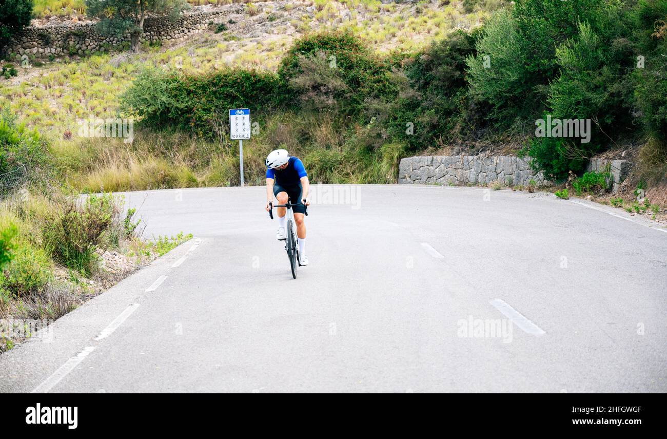 Unrecognizable cyclist climbing a hill on a mountain road looking back ...
