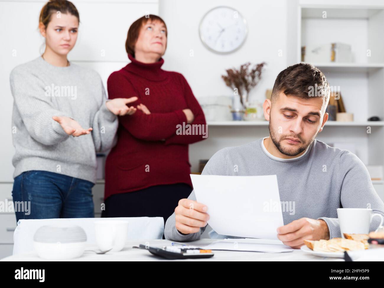 Distressed man with paperwork with irritated family behind Stock Photo ...