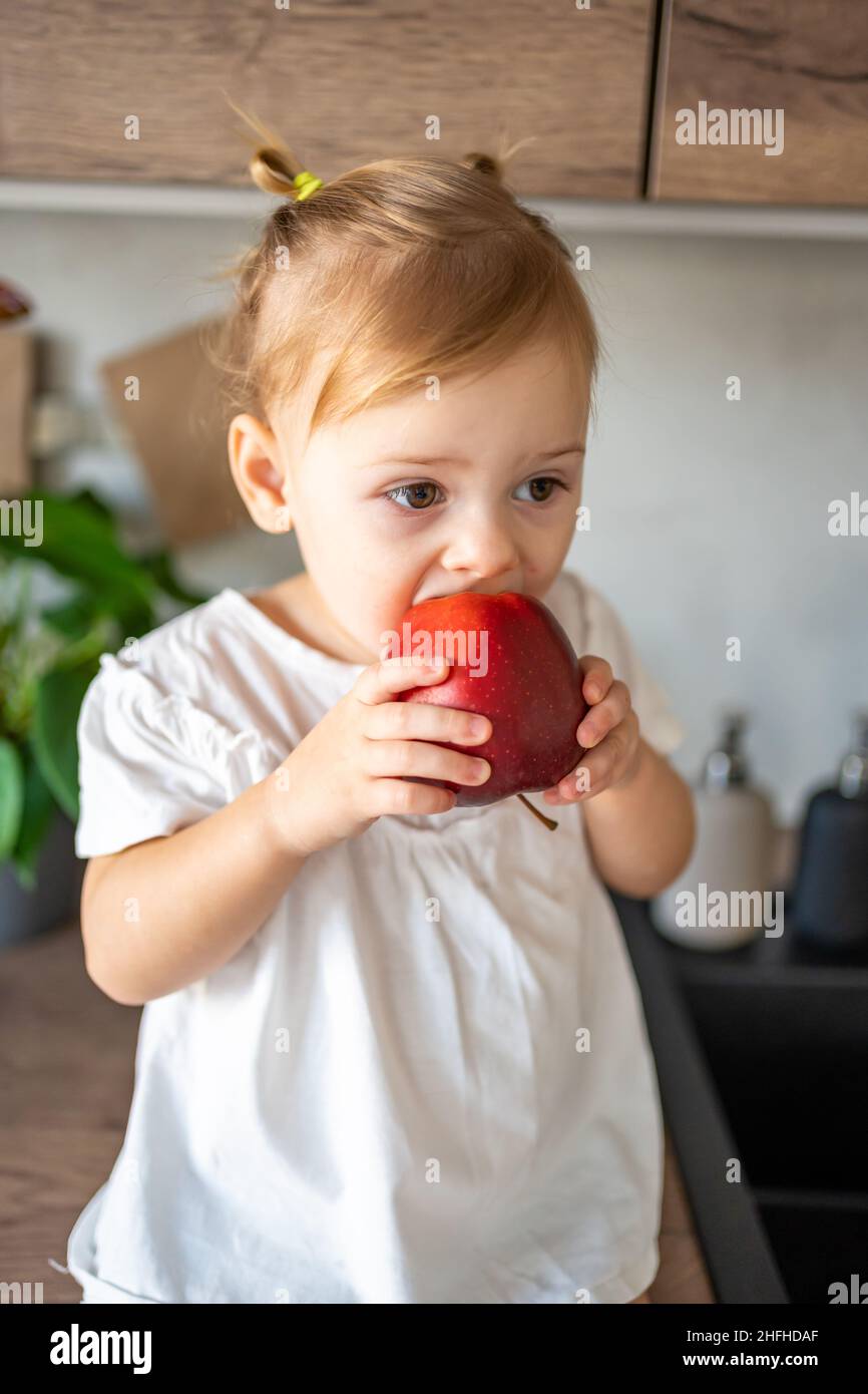 Baby girl blonde eating an apple in the kitchen, concept of healthy ...
