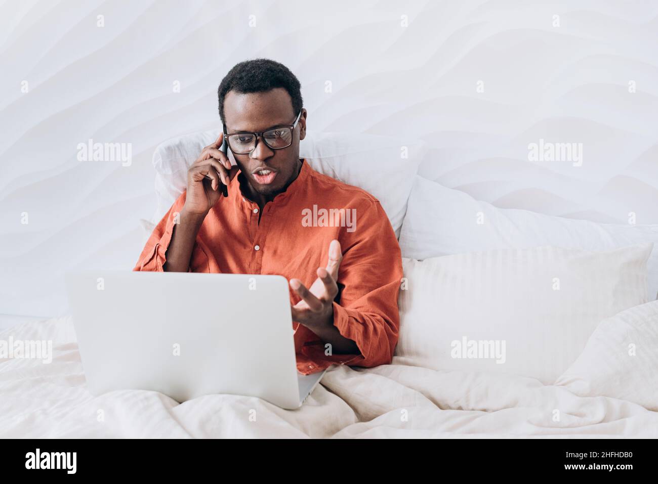Excited African-American man in orange shirt and glasses talks on ...