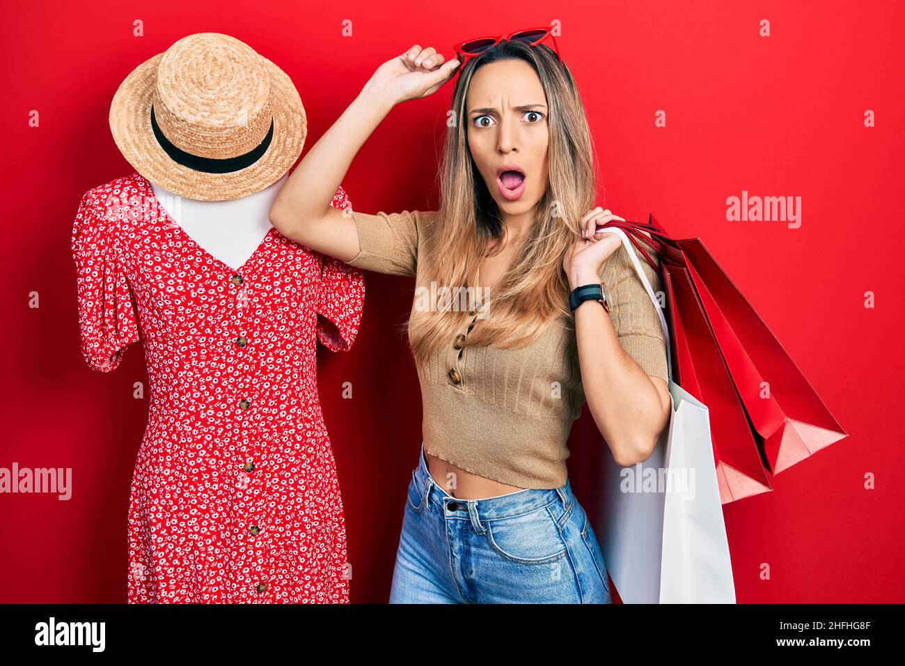 Beautiful hispanic woman holding shopping bags by retail manikin afraid ...