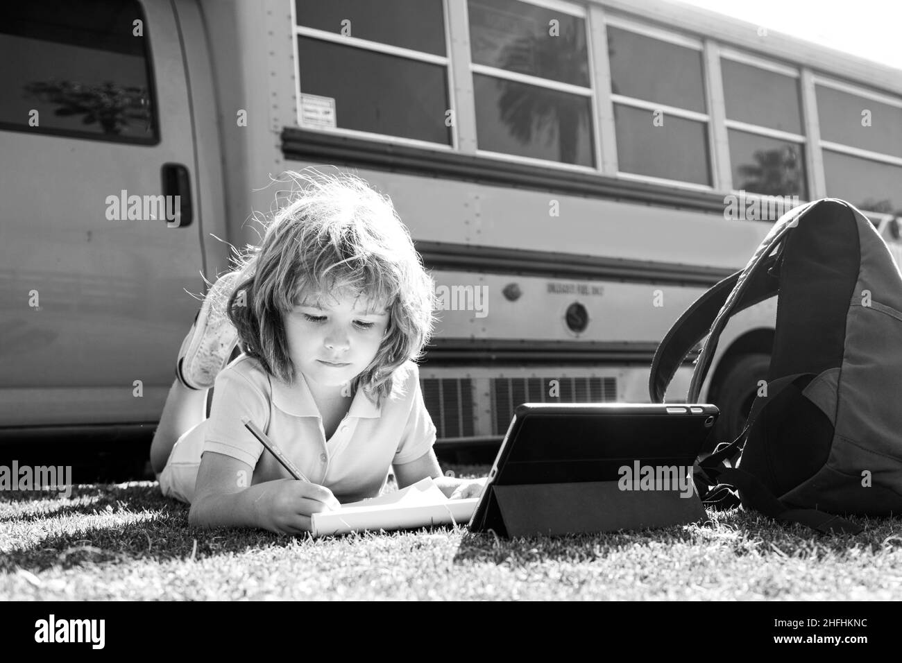 Smart schoolboy on laying on grass with digital tablet at school park ...