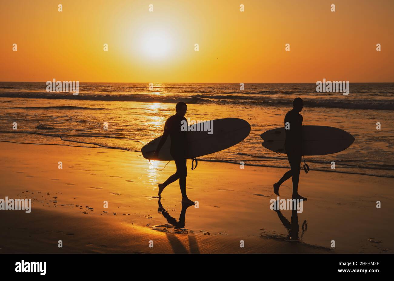 Silhouette of surfer people carrying their surfboard on sunset sea ...