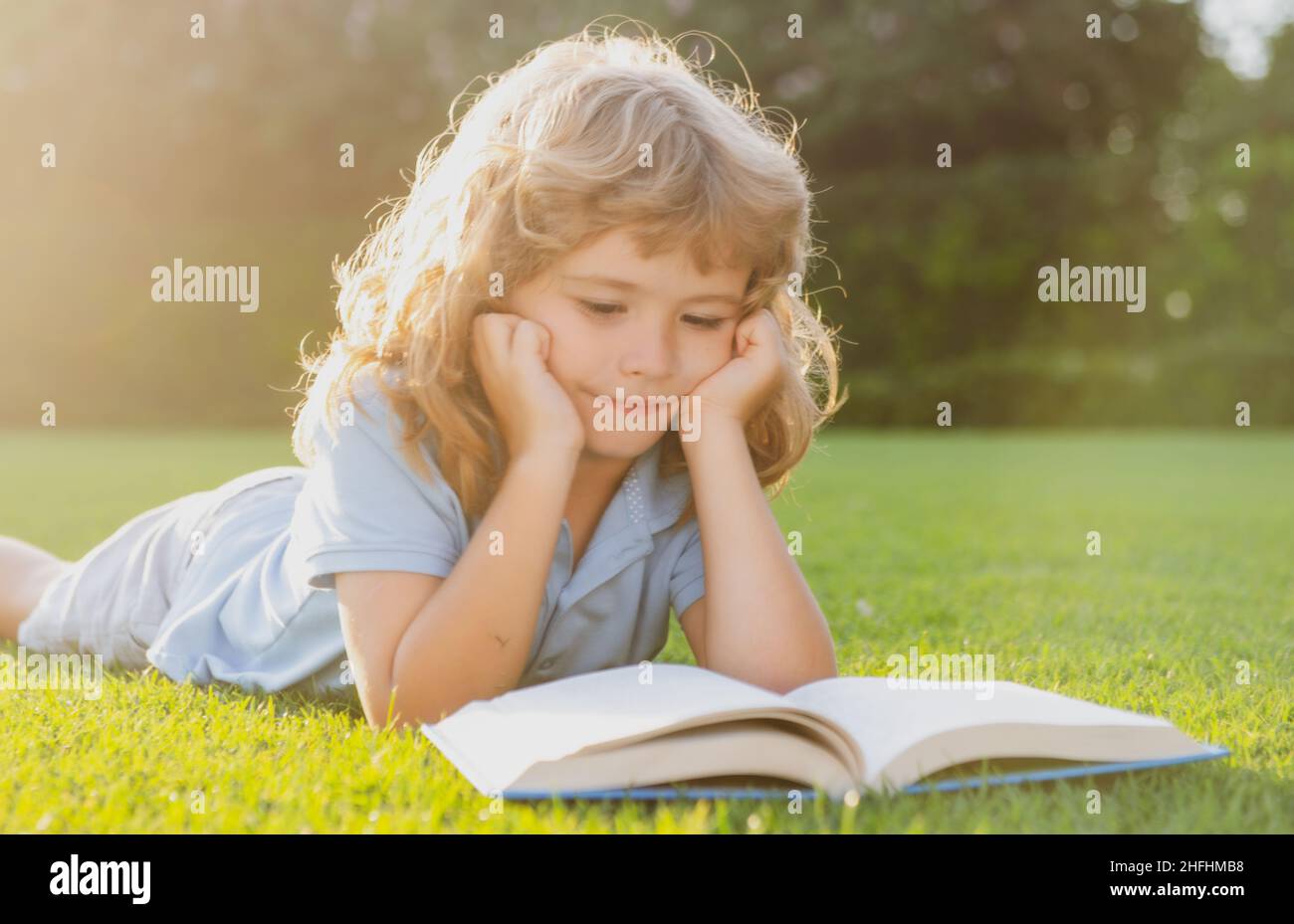 Kid boy reading a book lying on grass. Cute little child in casual ...