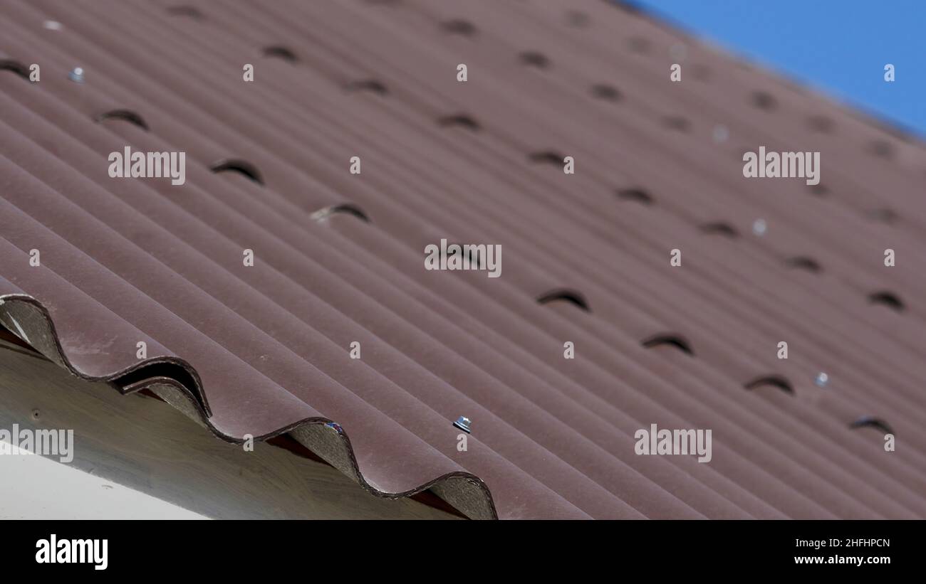 Roof with grey roof tiles and a clear blue sky with some clouds on a ...