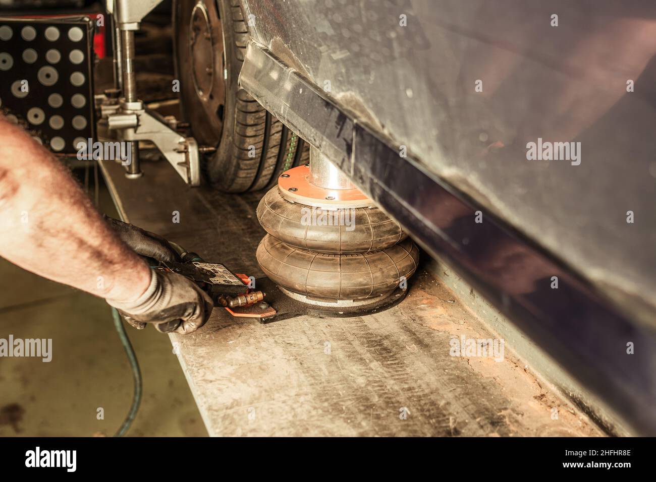 Mechanic placing a pneumatic jack under a car to lift it in a garage ...
