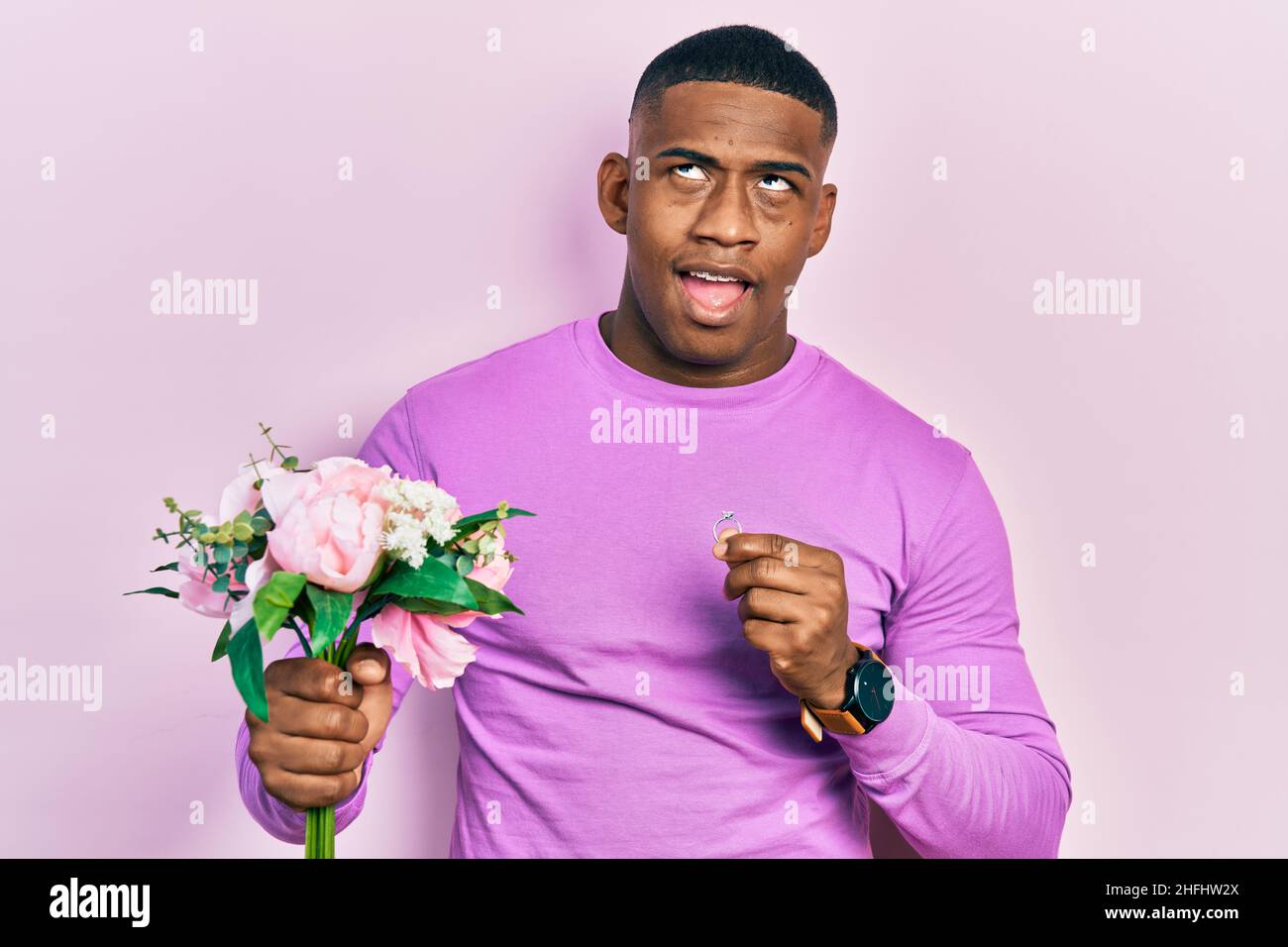Young black man holding bouquet of flowers and wedding ring angry and ...