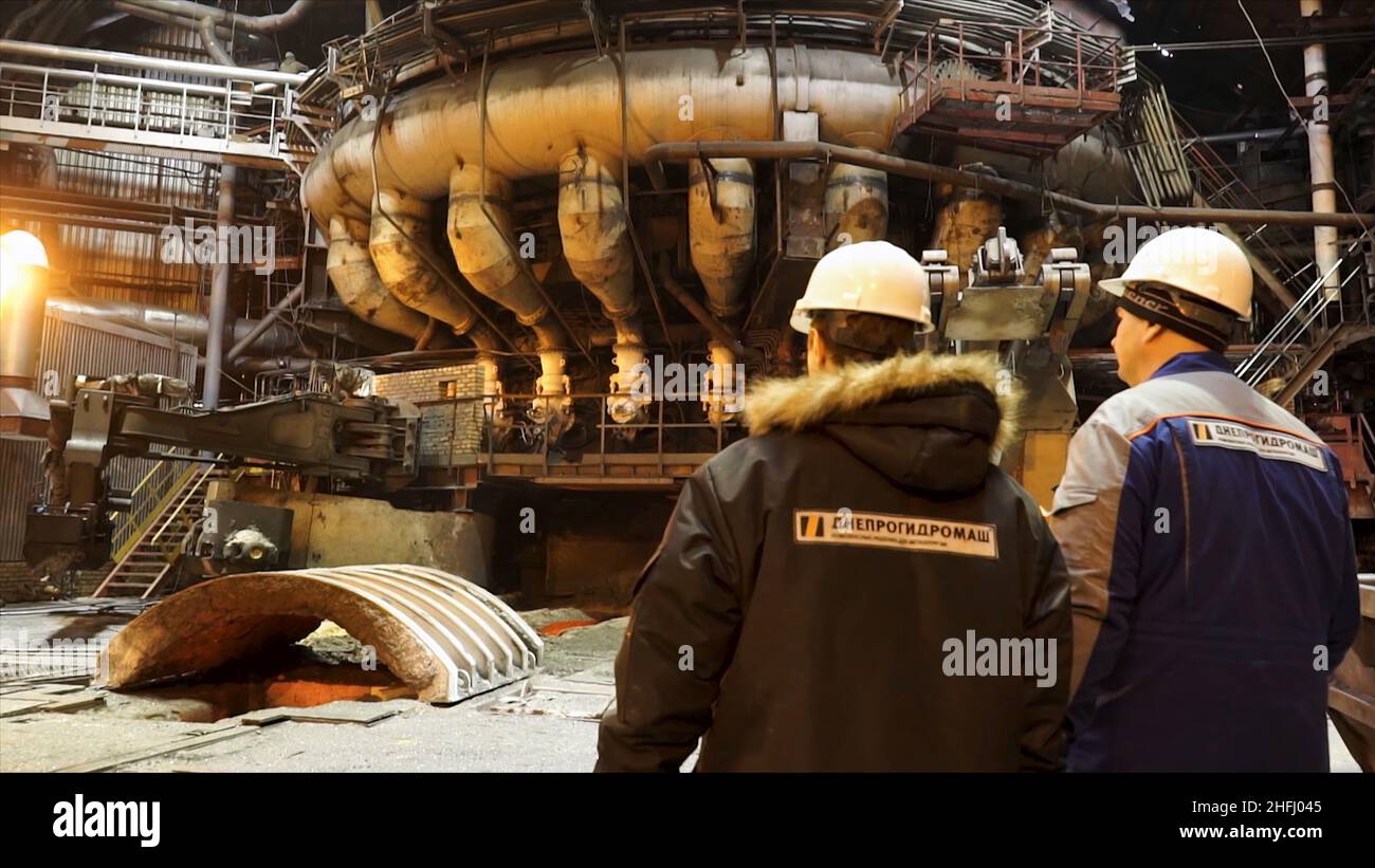 Rear view of two engineers looking at the giant blast furnace at the ...