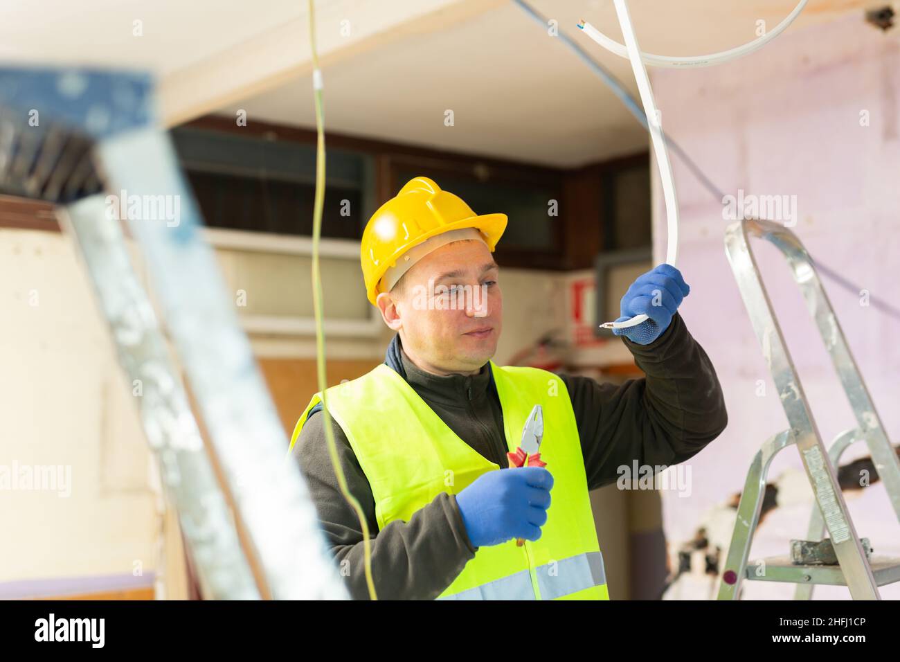 Electrician in protective uniform and helmet with pliers in his hands ...