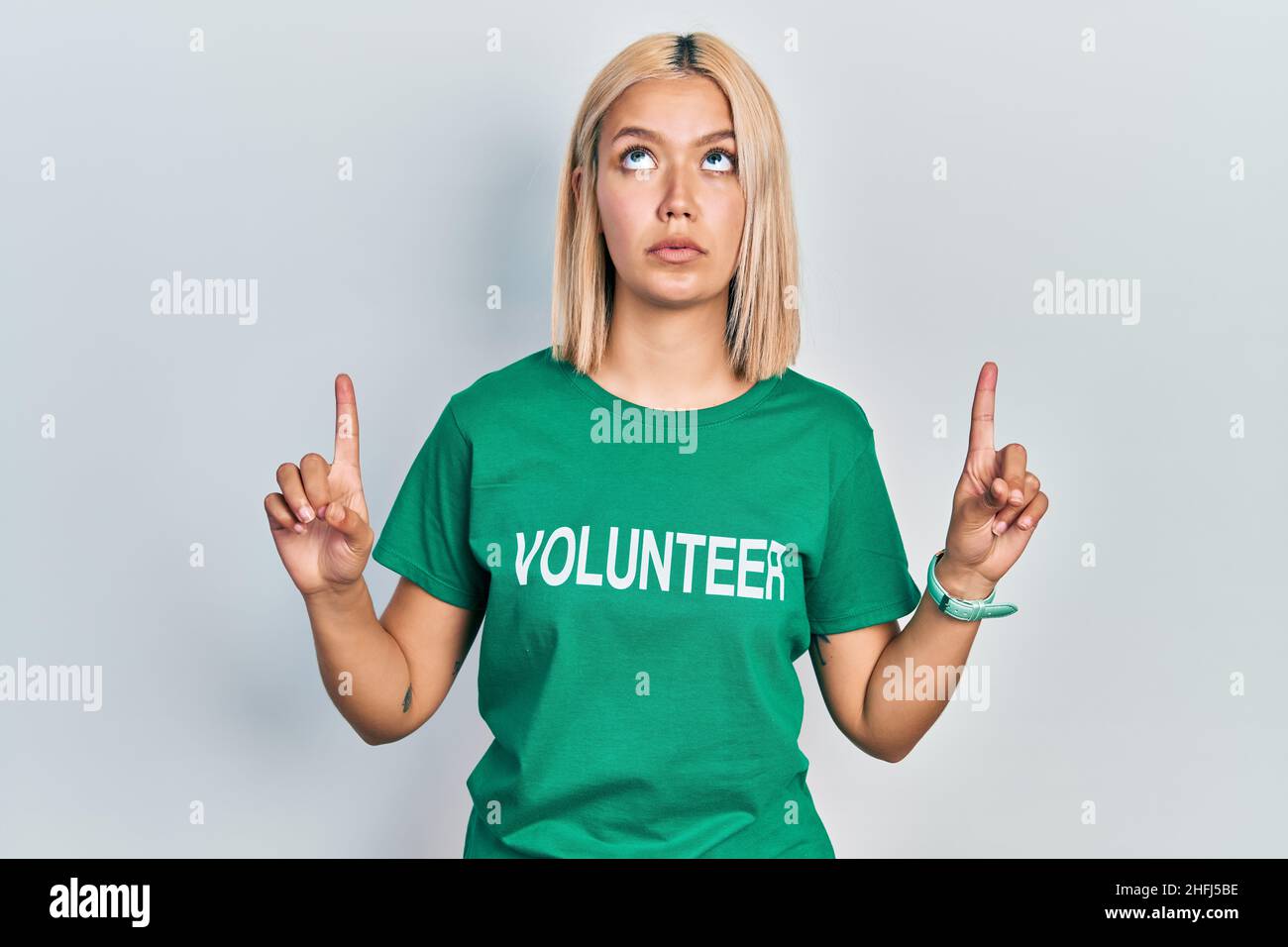 Beautiful blonde woman wearing volunteer t shirt pointing up looking ...