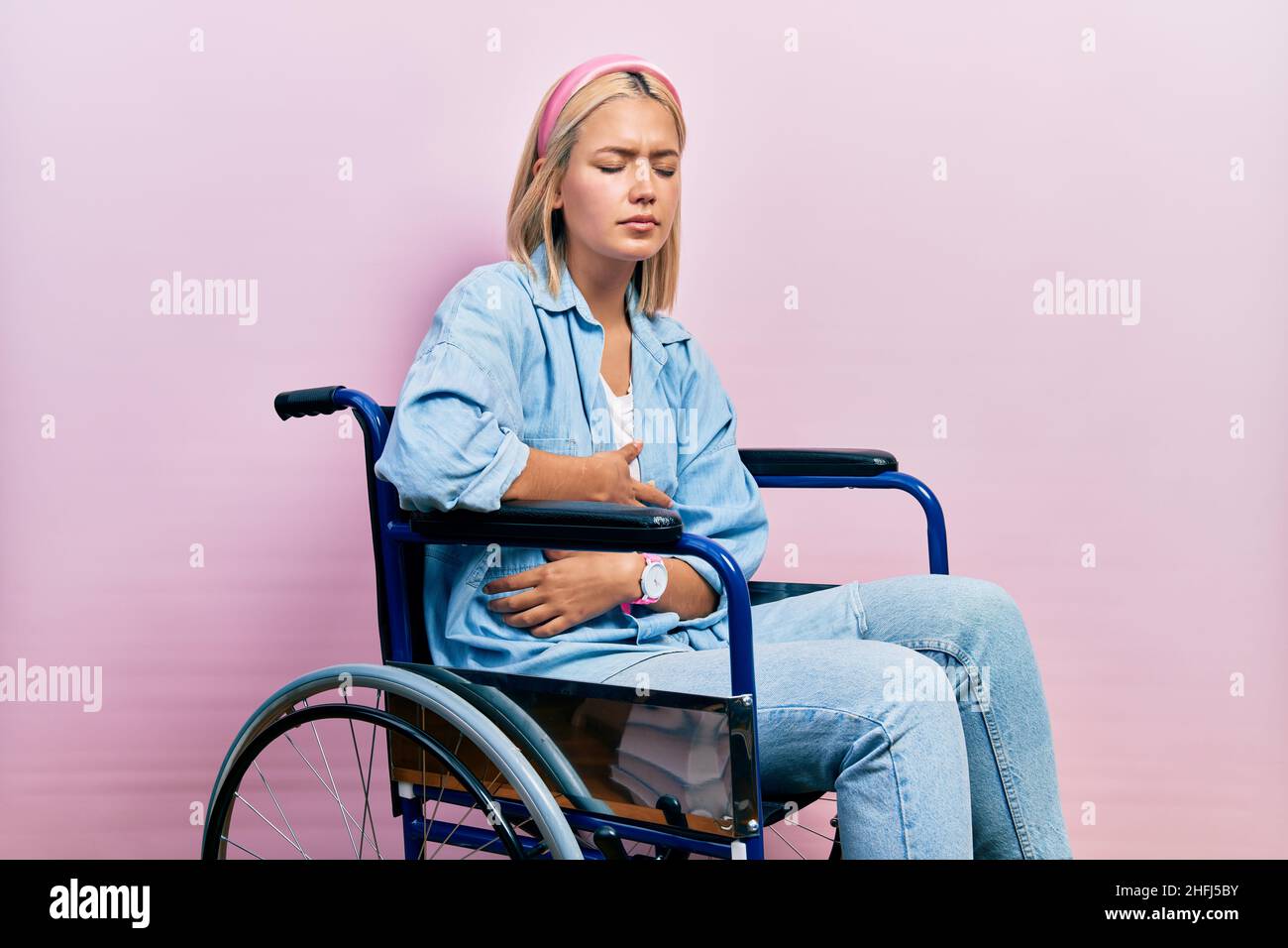 Beautiful blonde woman sitting on wheelchair with hand on stomach ...